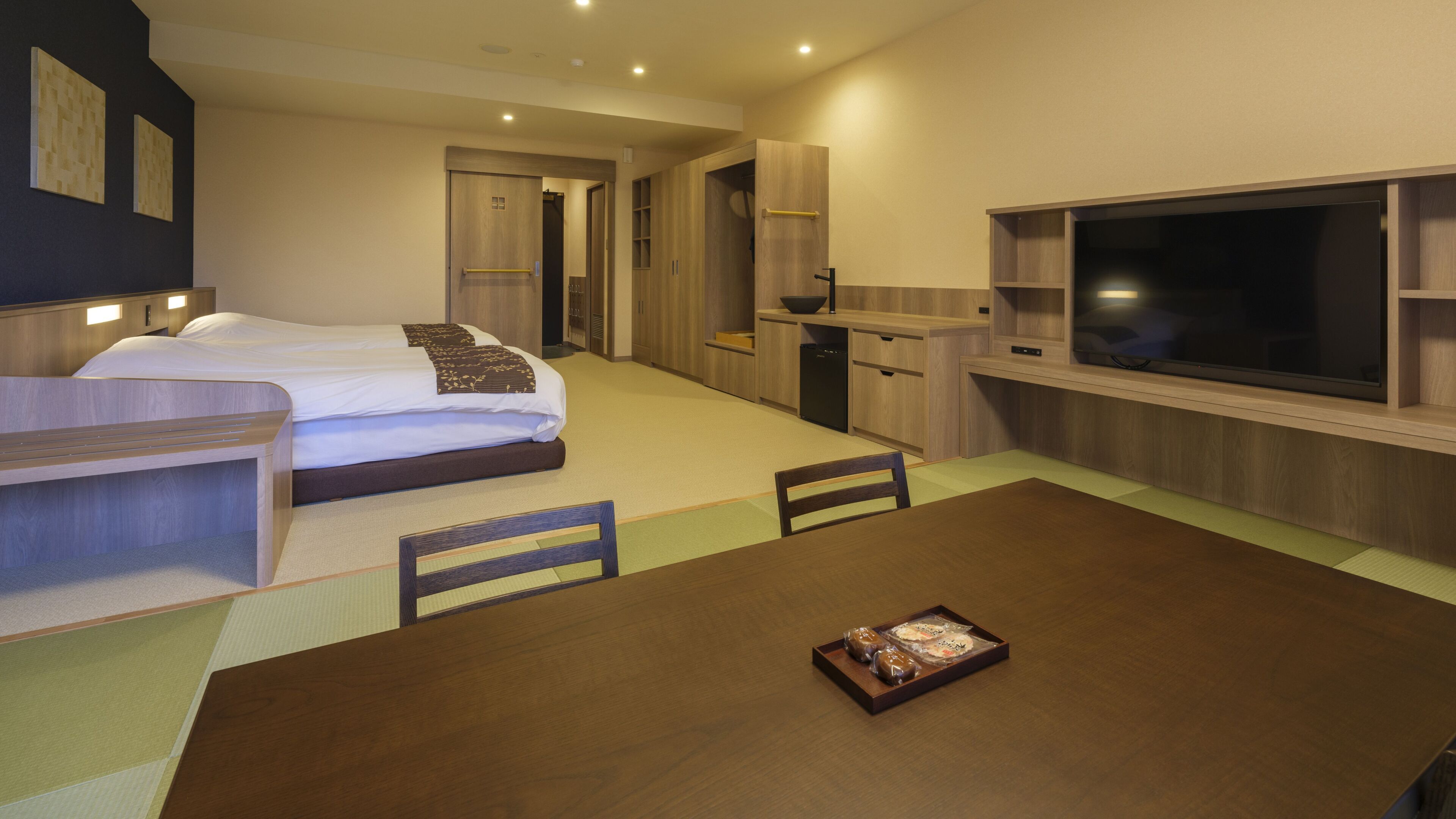 Quarto de hotel com cama, escrivaninha, mesa de jantar e televisão.