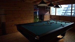 Uma mesa de bilhar em um salão com paredes de madeira e uma janela.