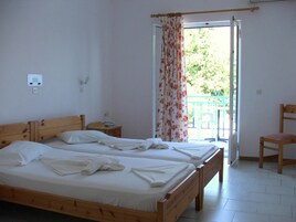 Quarto com duas camas de madeira, uma cadeira, uma mesa pequena e uma janela com cortina.