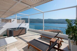 Uma varanda com hidromassagem, cadeiras de descanso e vista para o mar.