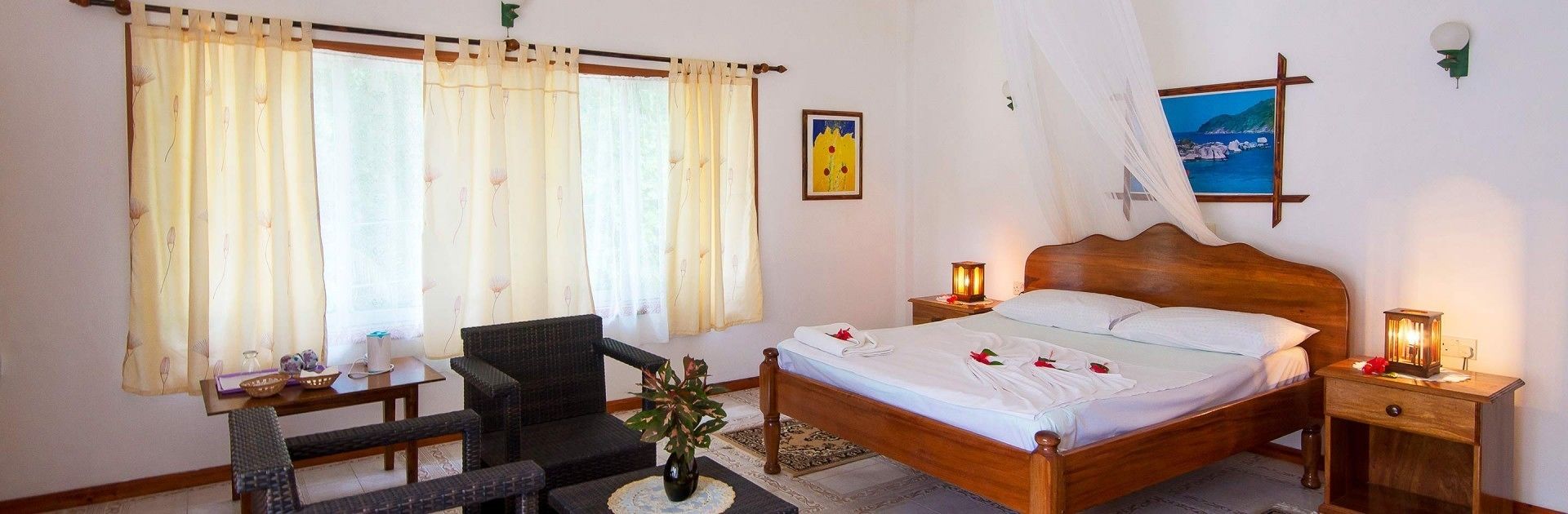 Um quarto com uma cama de madeira, duas mesas de cabeceira com luminárias, uma cadeira, uma pequena mesa com um vaso e uma janela com cortinas.
