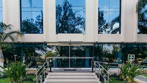 Um edifício moderno com fachada de vidro, entrada central com degraus e uma placa indicando uma clínica médica.