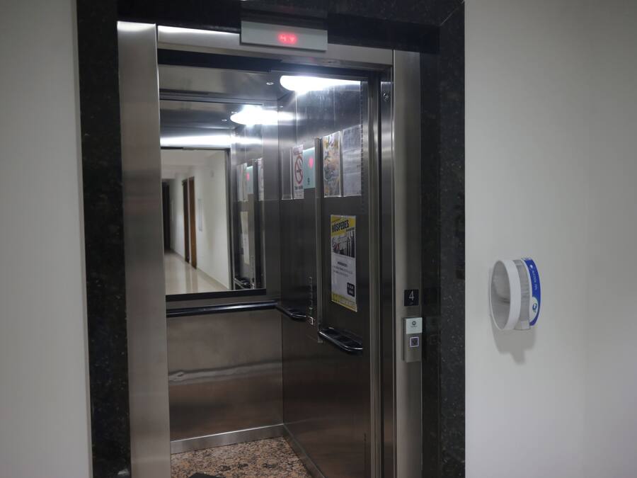 Interior de elevador com portas de aço inoxidável, corrimão, indicador de andar e placa com o número do andar.