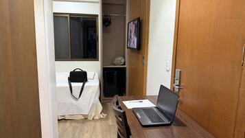 Quarto de hotel com uma cama, uma mesa de escritório com um laptop, uma televisão na parede e um guarda-roupa.