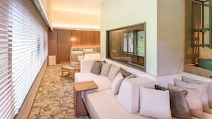 Quarto de hotel moderno com um sofá grande, uma cadeira de madeira e um espelho amplo.