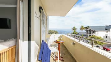 Uma varanda com vista para o mar, uma mesa com uma fruteira e uma cadeira.
