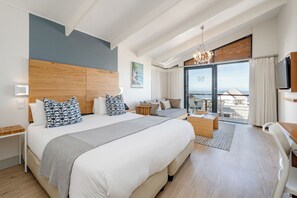 Quarto de hotel moderno com uma cama grande, uma varanda com vista e um espaço de refeições.