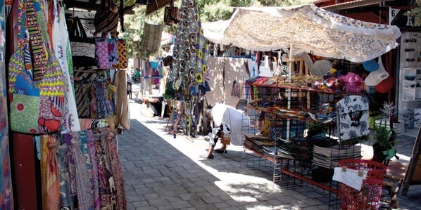 Rua estreita com lojas em ambos os lados, exibindo tecidos e artigos têxteis coloridos.