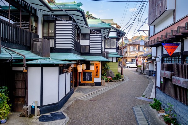 Uma rua estreita com edifícios tradicionais japoneses, uma pequena loja com uma placa e um carro estacionado.