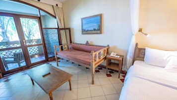 Quarto com cama, mesa, cadeira, mesinha com telefone e janela com vista para árvores.