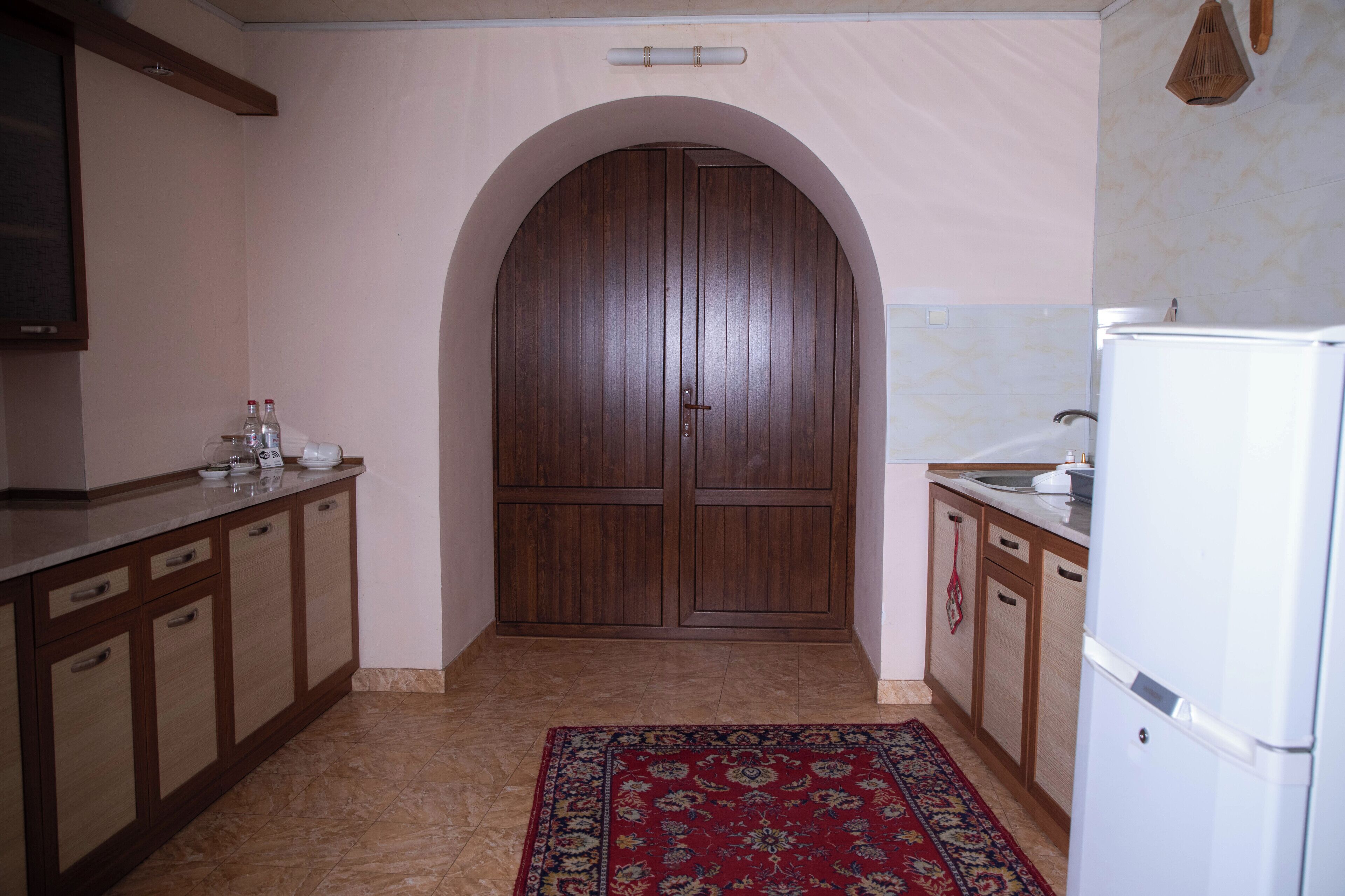 Uma cozinha com armários de madeira, porta dupla, geladeira e chão de azulejos.