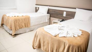 Duas camas de solteiro com roupa de cama branca e cobertores bege, uma mesa de cabeceira com telefone e uma cabeceira de madeira.