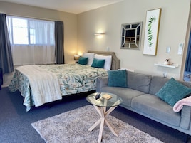 Quarto de hotel com uma cama, um sofá, uma mesa de centro de vidro e um tapete pequeno.