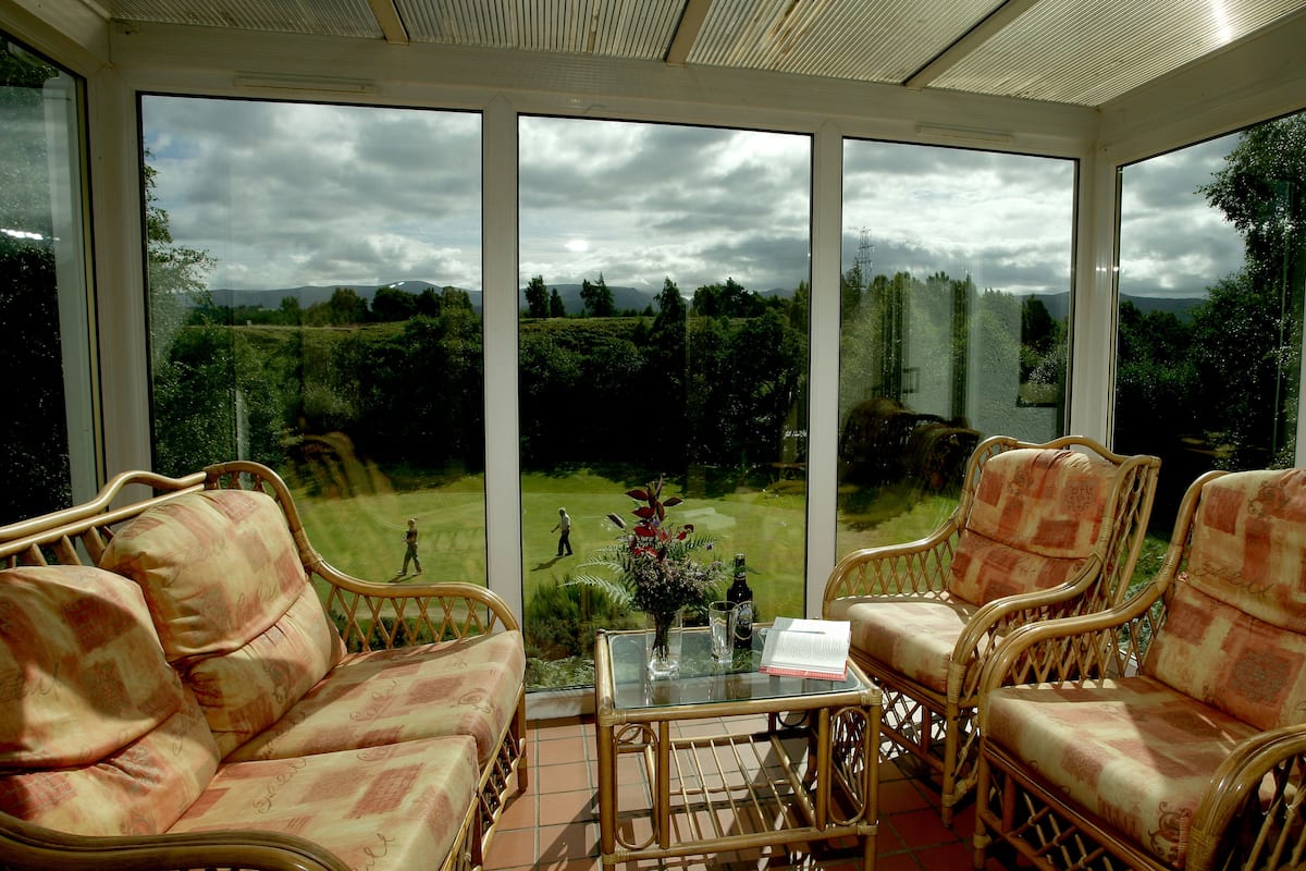 Uma estufa com mobiliário de vime, uma mesa de vidro e vista para um campo de golfe.