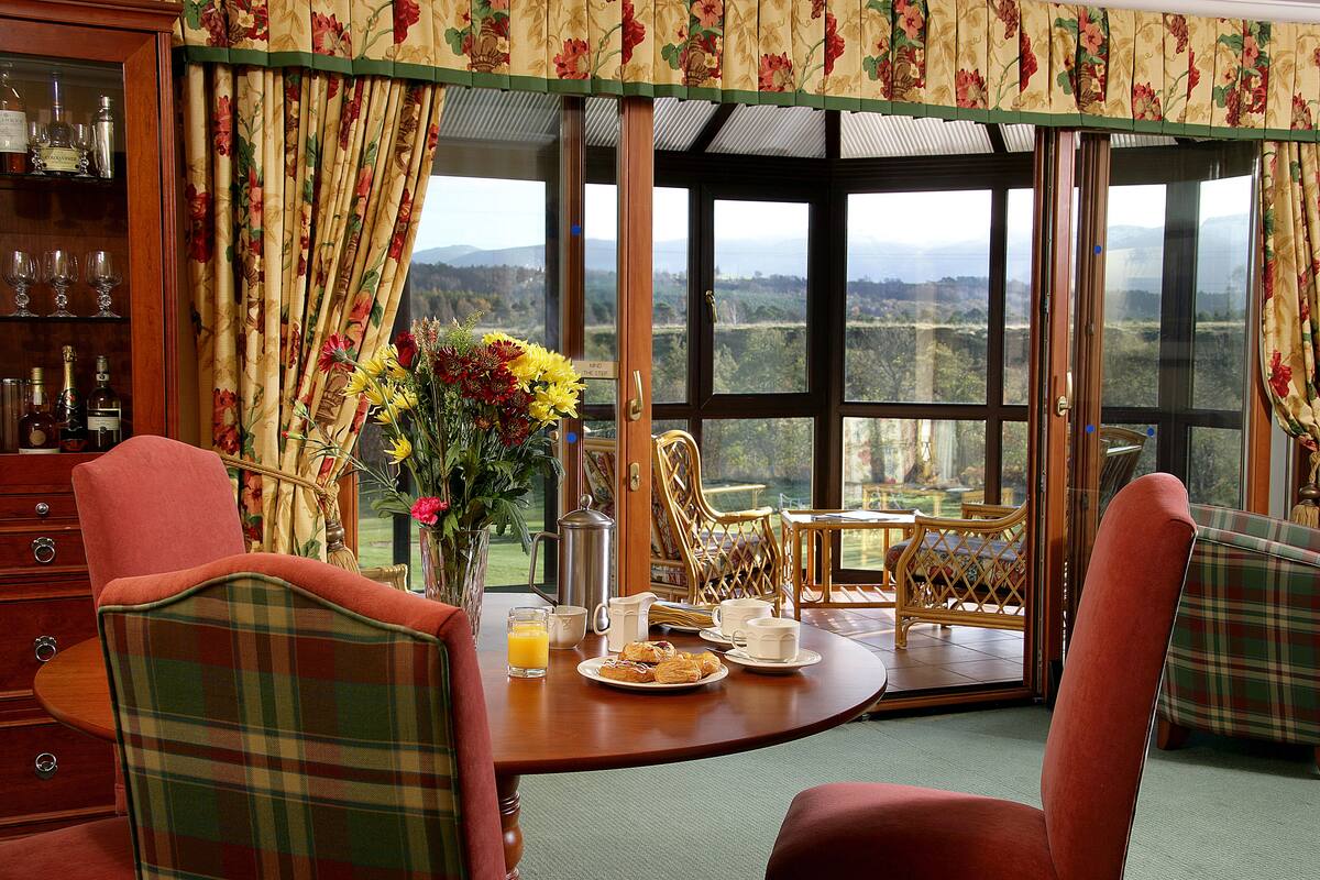 Uma área de refeições com uma mesa posta para o café da manhã, vista para o exterior e um armário de madeira com portas de vidro.