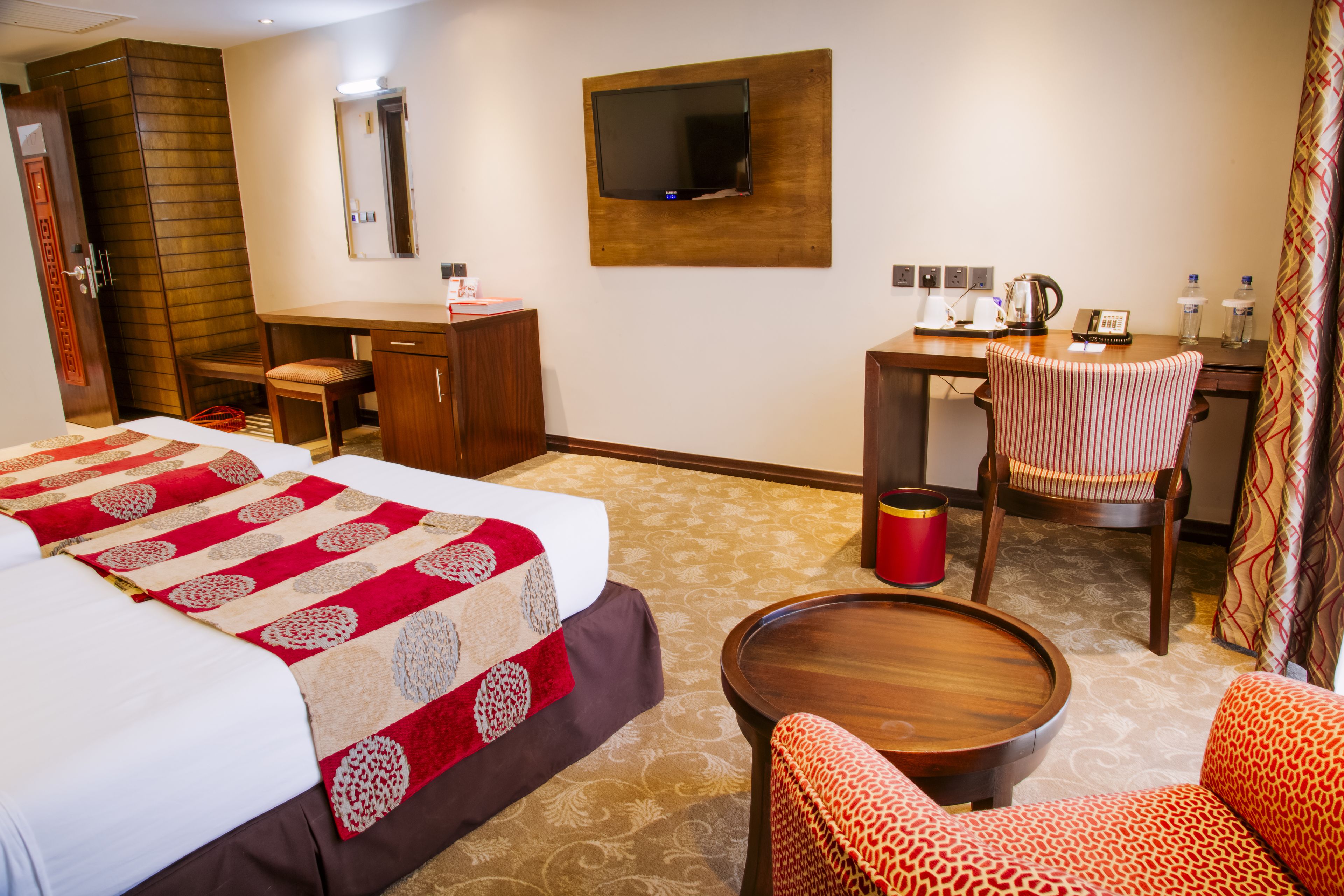 Quarto de hotel com cama, escrivaninha, cadeira, televisão e cafeteira.
