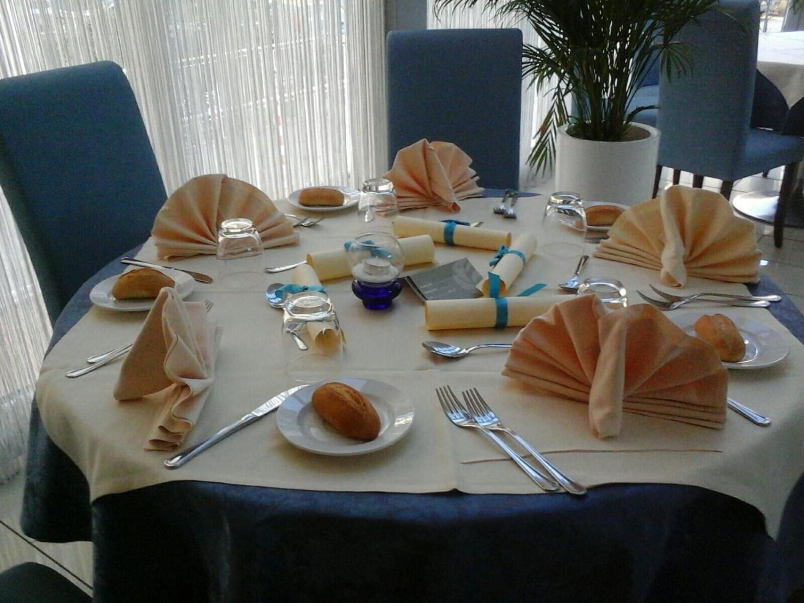Mesa de jantar posta com guardanapos dobrados, pratos, talheres e um copo de água.