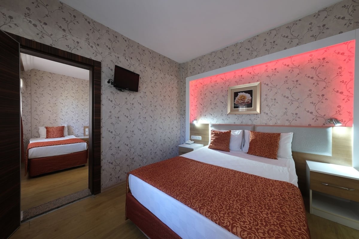 Quarto de hotel com cama, mesas de cabeceira, espelho e televisão na parede.