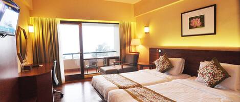 Quarto de hotel com duas camas, uma escrivaninha, televisão e varanda.