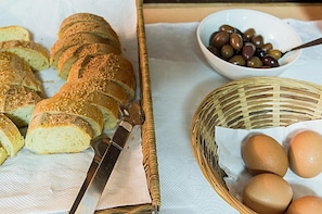 Fatias de pão, uma tigela de azeitonas e uma cesta de ovos sobre uma mesa.