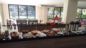 Um balcão de buffet com diversos alimentos e uma pessoa sentada à mesa ao fundo.