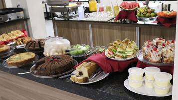 Buffet com diversos alimentos, incluindo bolos, pães e frutas.