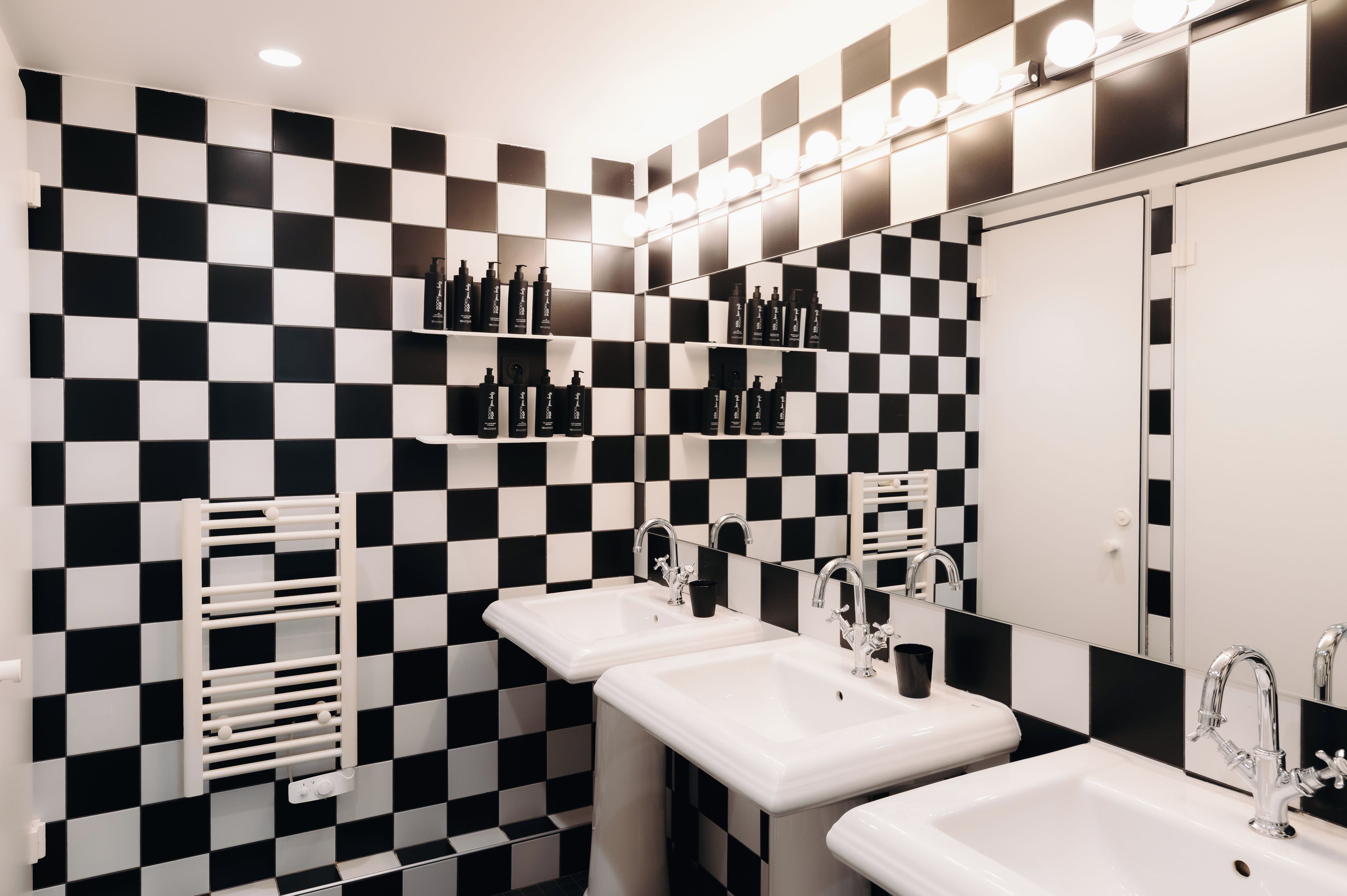 Casa de banho com azulejos a preto e branco, duas pias e um espelho.