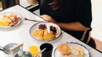 Uma pessoa sentada à mesa com itens de café da manhã, como croissants, feijão e pão, além de uma xícara de café.