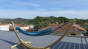 Uma rede em um terraço com vista para a paisagem urbana e colinas ao fundo.
