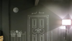Pared preta com desenho de giz de uma porta com a inscrição “guest house”, uma pequena lua e um abajur.