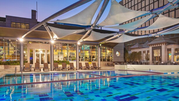 Uma piscina com um padrão geométrico de azulejos, ladeada por espreguiçadeiras e com grandes toldos brancos para sombra.