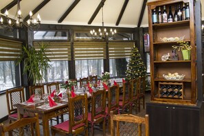 Uma área de jantar com mesas e cadeiras de madeira, um pinheiro de Natal e um suporte para vinhos.