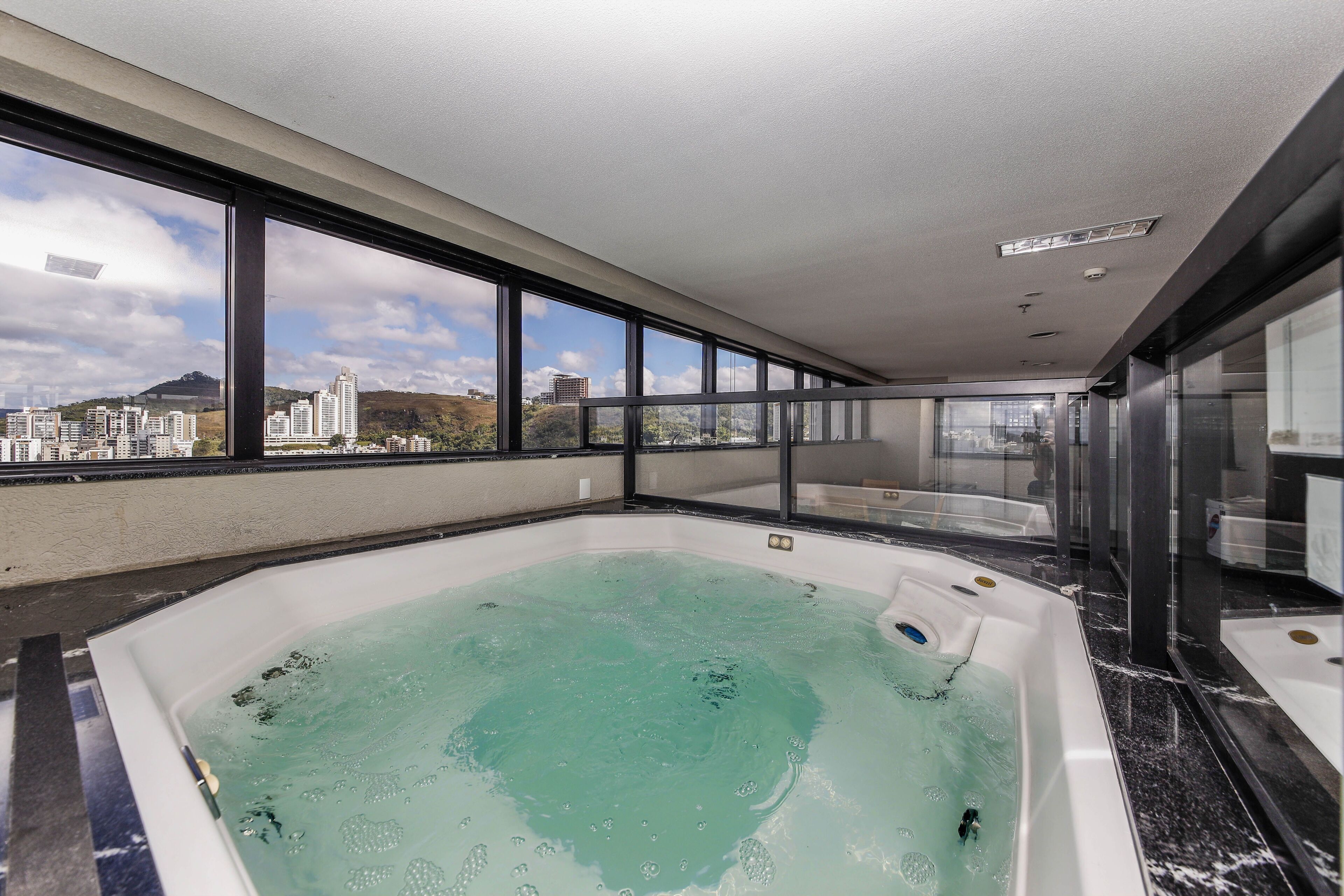 Uma banheira de hidromassagem grande e coberta, com vista para a cidade, divisória de vidro e design de interiores moderno.
