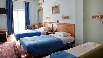 Quarto de hotel com duas camas, uma escrivaninha, uma cadeira, televisão e janela com cortinas.