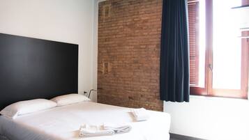 Quarto de hotel com uma cama, parede de tijolos e janela com persianas.