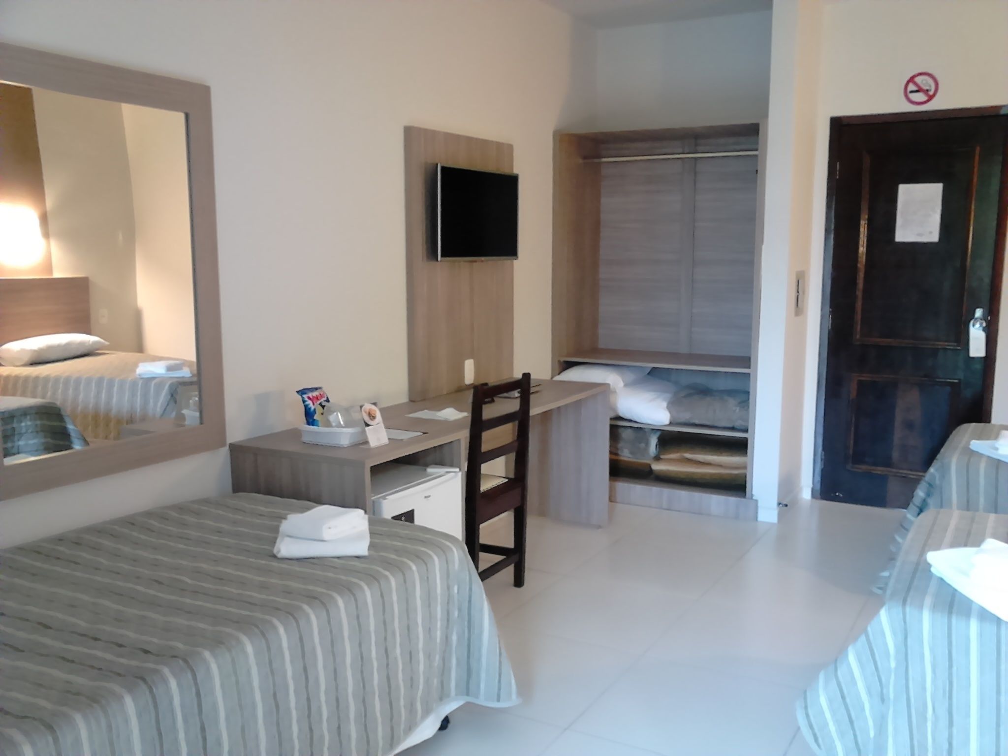 Quarto de hotel com duas camas, uma escrivaninha, uma cadeira, televisão e guarda-roupa.