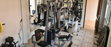 Academia com diversos equipamentos de exercício, um espelho e piso revestido de azulejos.