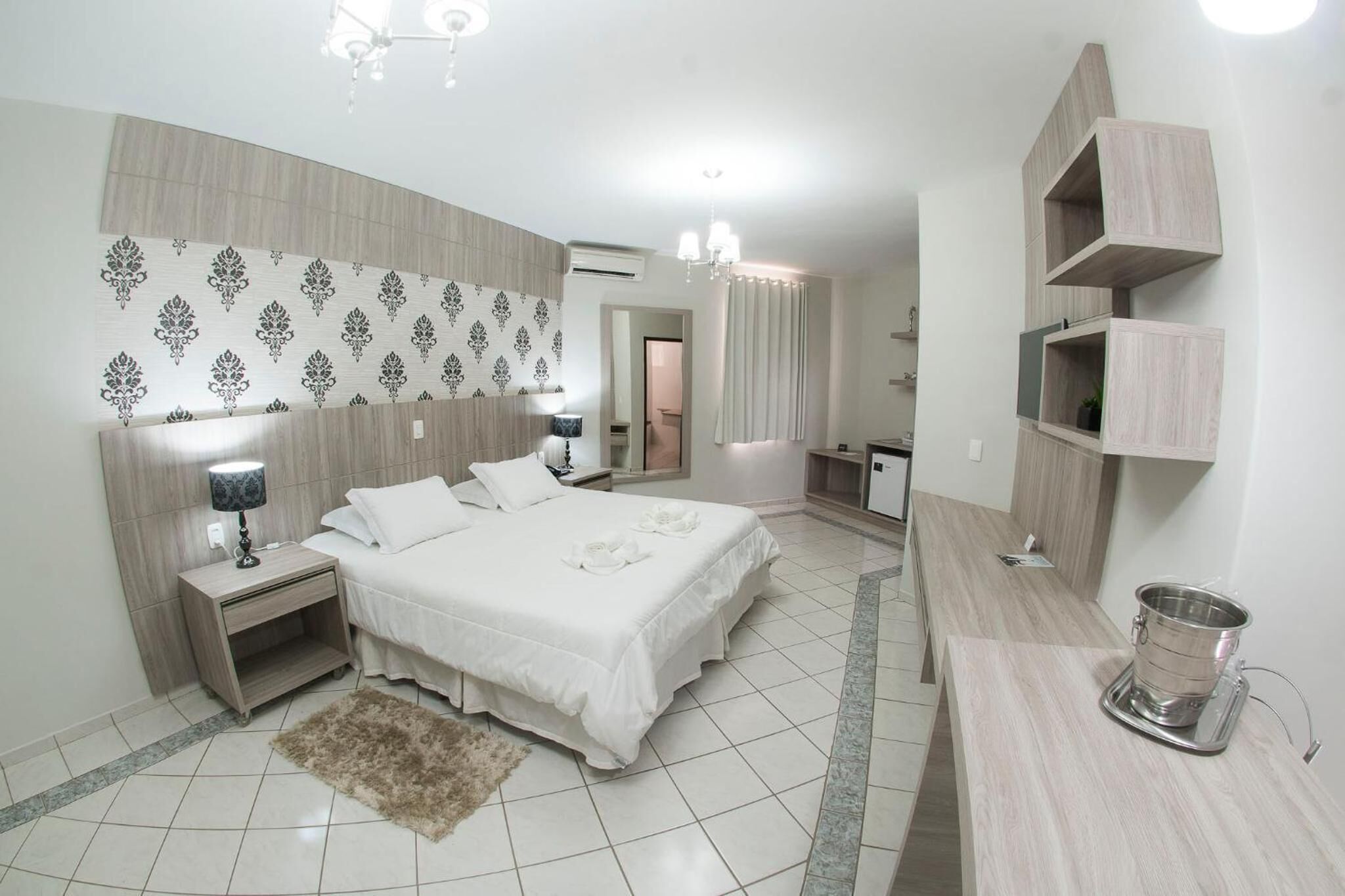 Quarto moderno com uma cama grande, mesas de cabeceira, escrivaninha e estantes embutidas.