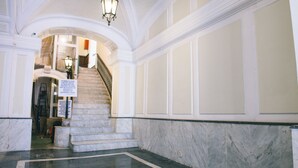 Um corredor com piso de mármore, uma escadaria, uma placa e um lustre.