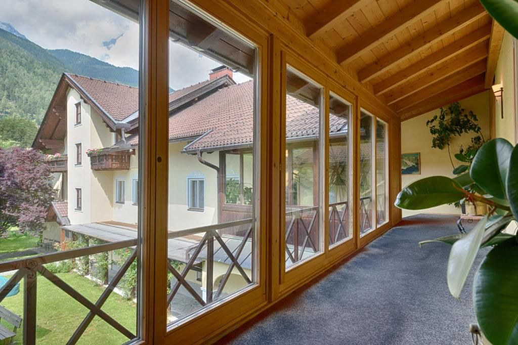 Quarto com grandes janelas, vigas de madeira e vista para uma casa e montanhas.