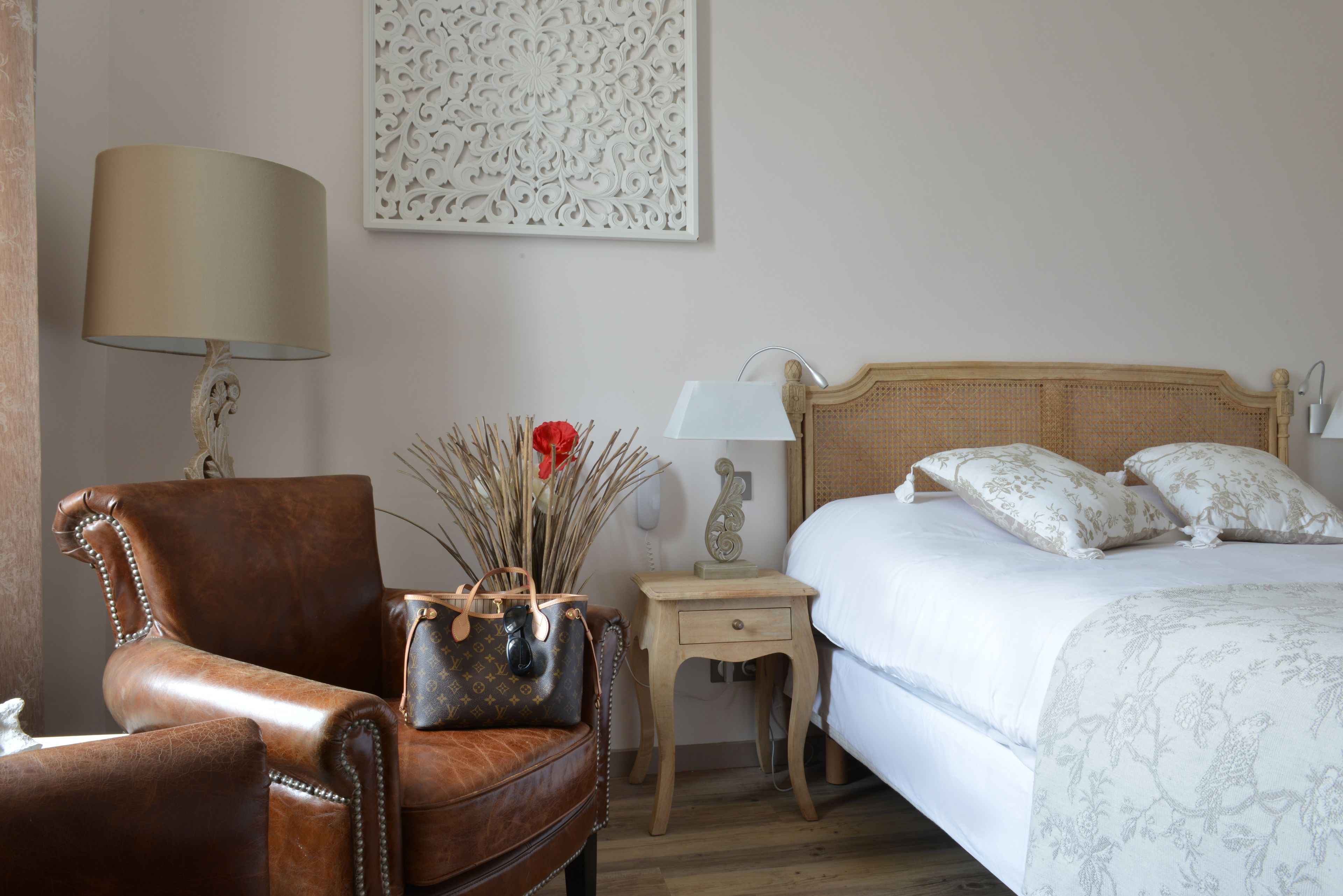 Quarto com cama, mesa de cabeceira, abajur, cadeira e um objeto decorativo na parede.