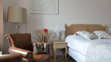 Quarto com cama, mesa de cabeceira, abajur, cadeira e um objeto decorativo na parede.