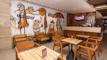 Um restaurante com mesas e cadeiras de madeira, um mural na parede e uma tela de televisão exibindo um anúncio de pizza.