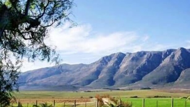 Uma área de refeições com mesa e cadeiras, com montanhas e céu claro ao fundo.