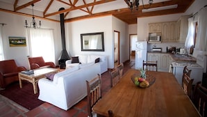 Uma sala de estar acolhedora com lareira, uma mesa de jantar com frutas e uma cozinha com armários de madeira e fogão.