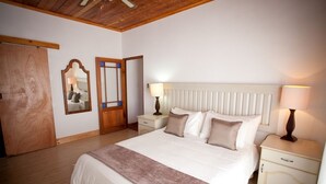 Quarto com uma cama grande, teto de madeira, paredes brancas e uma porta de madeira.