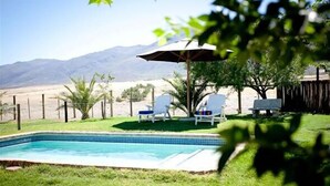 Piscina com espreguiçadeiras e guarda-sol, cercada por vegetação e uma paisagem desértica ao fundo.