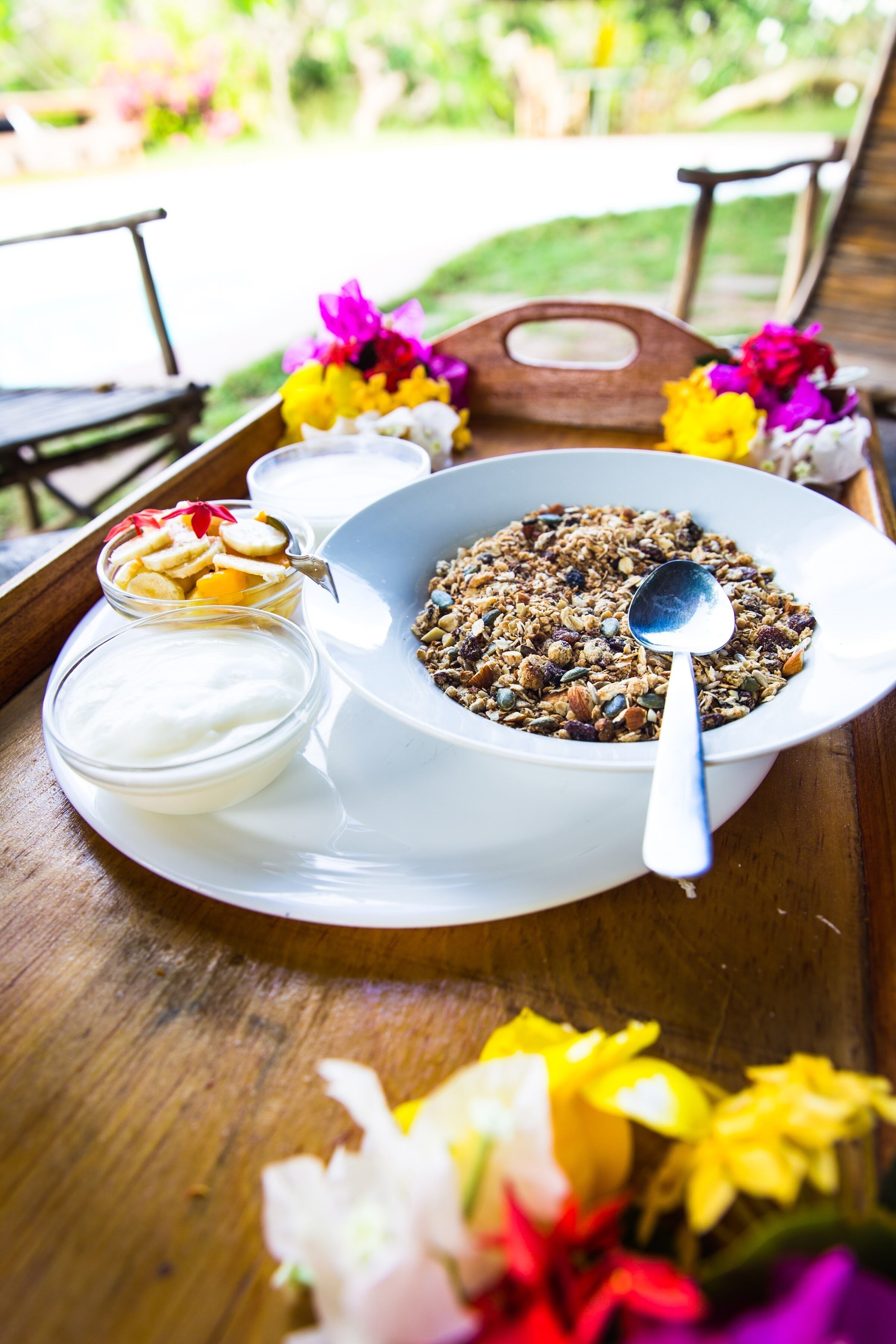 Bandeja de café da manhã com um pote de granola, iogurte e frutas em uma mesa de madeira.