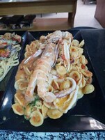 Prato de frutos do mar com massa e um lagostim grande numa bandeja preta.