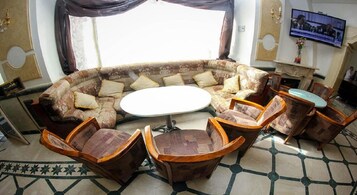 Uma sala de estar com um amplo sofá em formato de L, uma mesa de centro redonda e cadeiras de madeira.